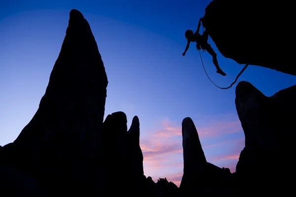 Rock climber dangling by one arm. - Stock Image - Everypixel